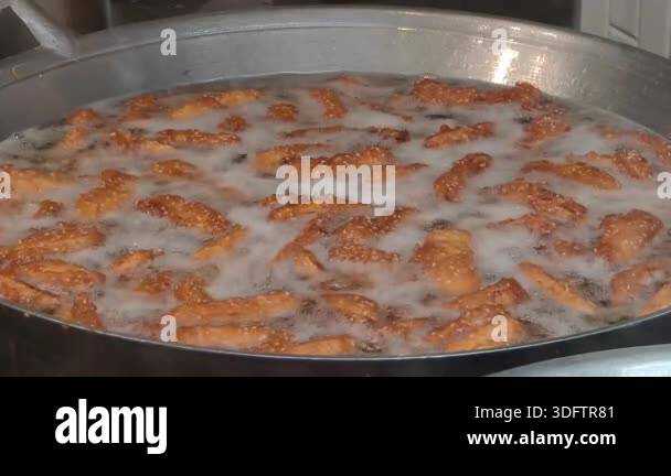 Deep-fried bananas with sesame seeds bubbling in hot oil in large metal ...