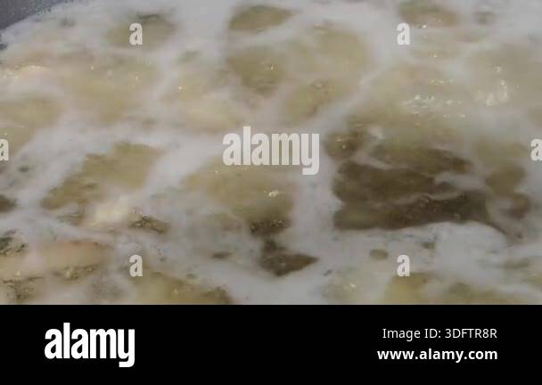 Deep-fried bananas with sesame seeds bubbling in hot oil in large metal ...