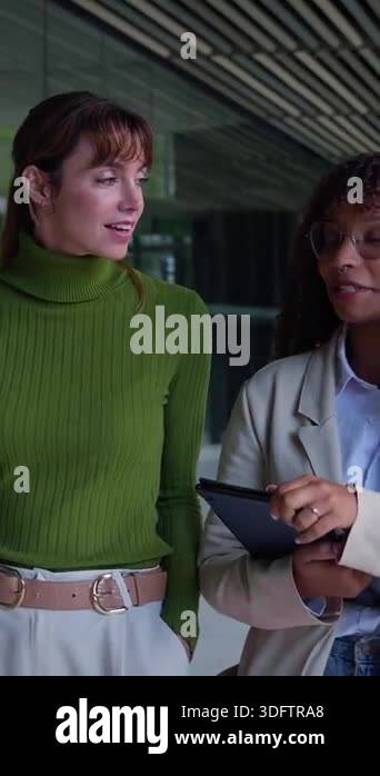 Vertical. Two colleagues walk past a modern glass building while ...