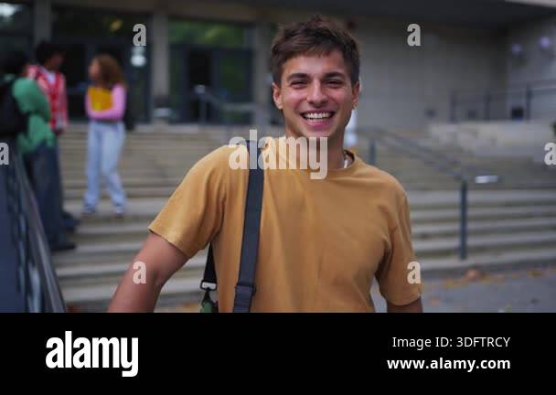 Smiling caucasian student looks at the camera on campus steps, carrying ...
