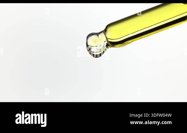 Slow motion video of golden cosmetic oil dripping from a glass pipette ...