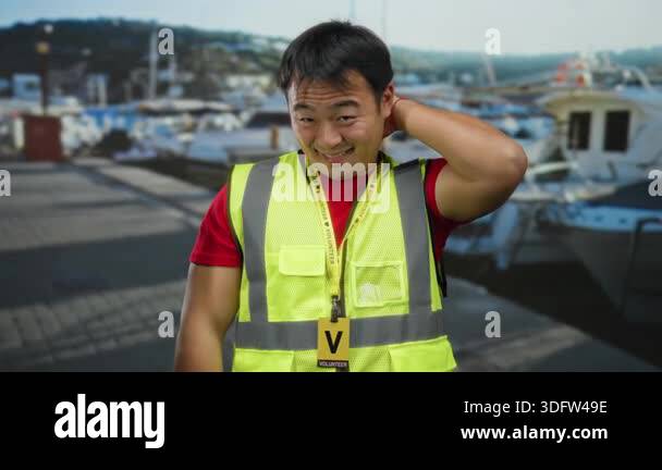 Asian man in reflective vest smiling at seaside port with boats under ...