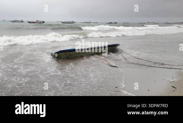 Small boat washed ashore by large waves during a storm on a rainy day ...