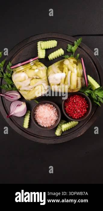Glass jars with pickled cucumber and onion salad rotating on a dark ...
