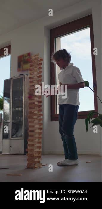 Child places wooden piece onto high block stack showing risk awareness ...