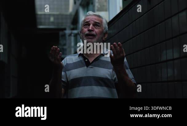 Senior man looks upward with arms extended, expressing vulnerability ...