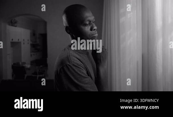 African American man standing by window indoors in quiet contemplation ...