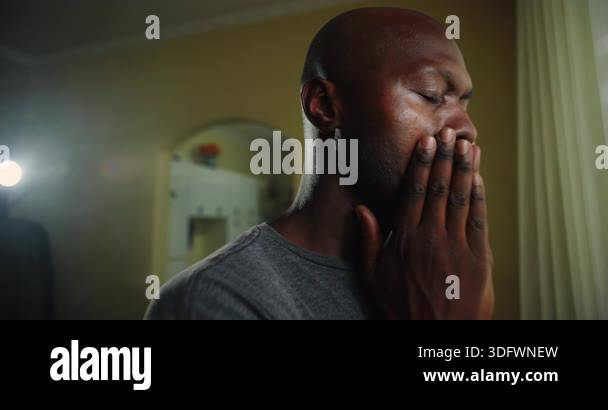African American man standing by window covering mouth, anguish, quiet ...