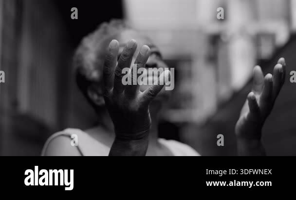 Senior woman raises open palms in prayer in black and white, expressing ...