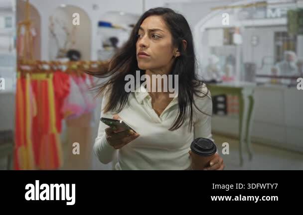Woman holding a ribbed takeaway coffee cup and smartphone, frowning and ...