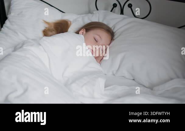 A young child rests peacefully in bed, cocooned in soft white blankets ...