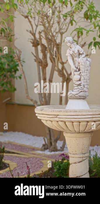 Stone fountain with female statue in sunny garden with blooming flowers ...