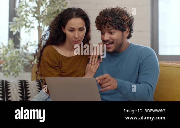 A couple sits closely on a couch, sharing an exciting moment as they ...