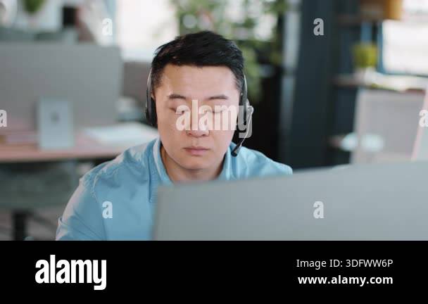A man wearing a headset sits at a desk in a contemporary office. He has ...