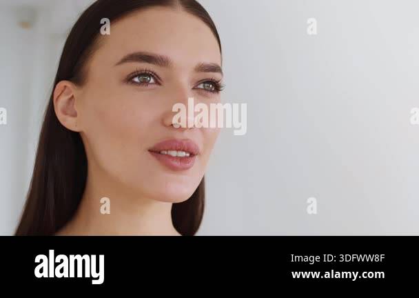 A young woman stands in bright light, displaying a serene expression ...