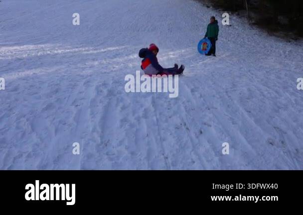 Young girl sledding fast down a snowy winter slope on a plastic sled ...