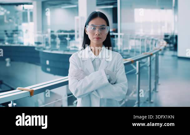 A focused woman in a lab coat stands confidently in a modern laboratory ...