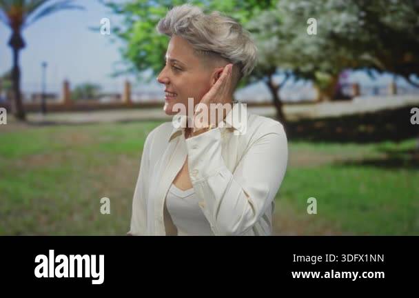 Woman with short hair covers ears under flowering tree in green park ...
