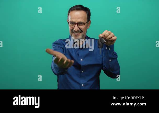 Man holding car keys smiling on green background wearing blue shirt ...