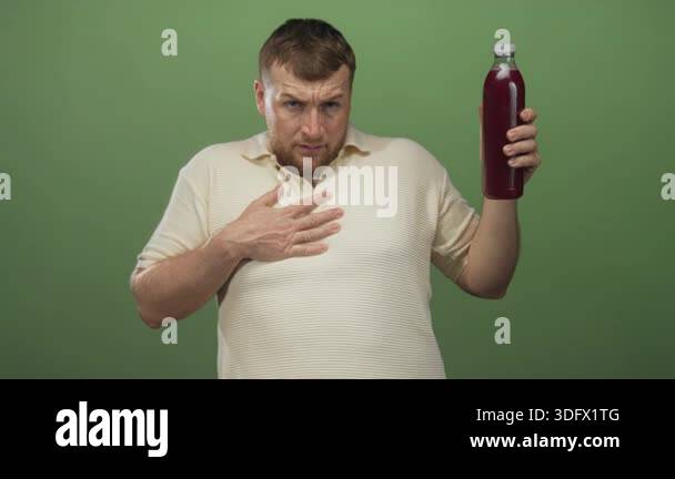 Man holding bottle with hand on chest in green studio showing maroon ...