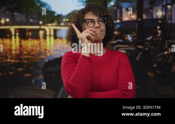 Woman standing by canal water on city street with hand on chin under ...