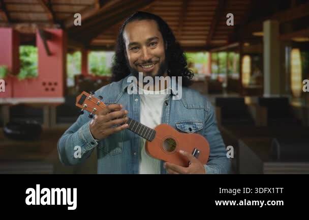 Man smiling and strumming a ukulele with hands on the fretboard ...
