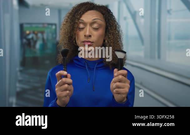 Transgender woman holds makeup brush and examines bristles in airport ...