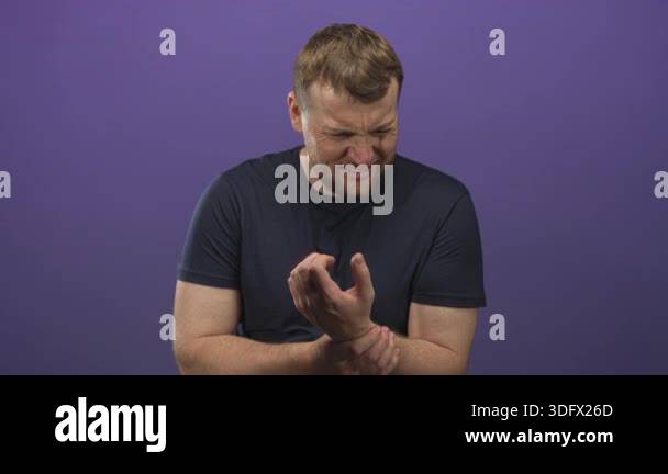 Young man clutching his wrist and wincing with visible hand pain in a ...