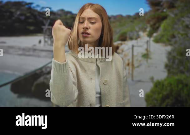 Young blonde woman wears knit cardigan and taps a raised fist against ...