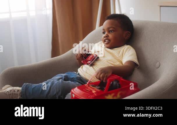 A smiling young boy relaxes on a comfortable chair while playing with ...