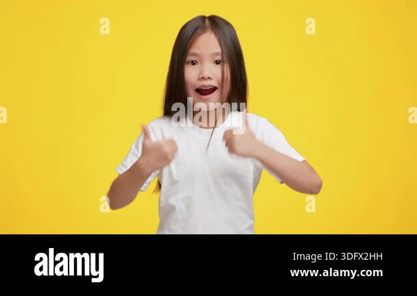A joyful child with straight black hair is giving a thumbs up while ...