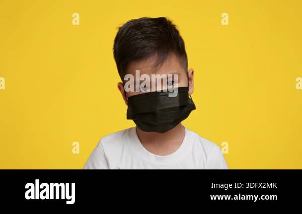 Young child with black mask gazes thoughtfully against a vibrant yellow ...