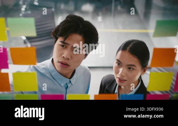 Two young Asian professionals engage in a brainstorming session as they ...
