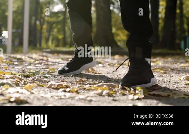 A young man runs along a tree-lined street covered in fallen leaves ...