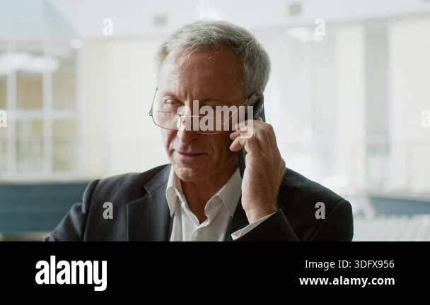 An elderly man in a suit is on a phone call in a modern office. He ...