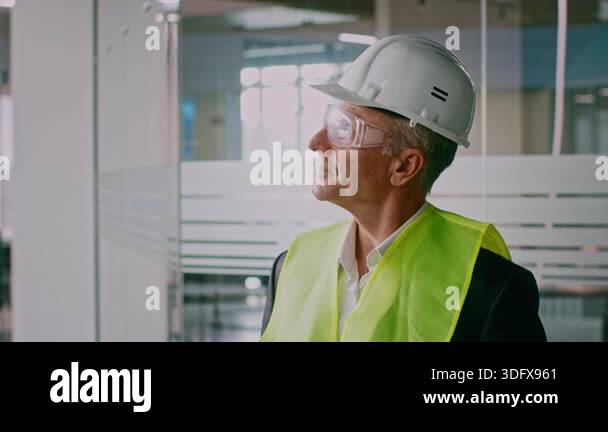 A senior man in a yellow safety vest and hard hat engages in ...