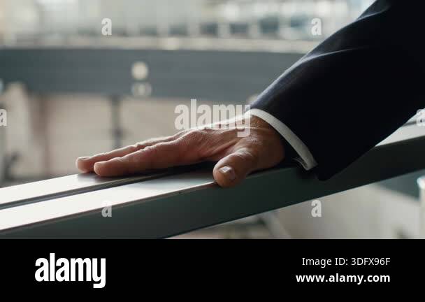 An elderly man in a suit leans on a railing in a contemporary office ...