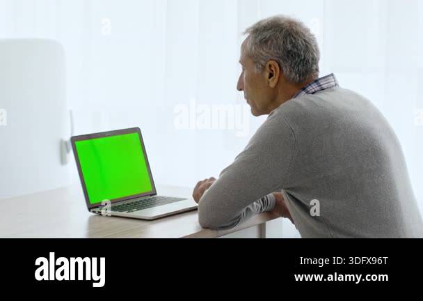 An elderly man in his 60s sits at a table, focusing intently on a ...