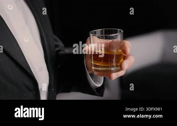 An elderly man in a suit holds a glass of whiskey, exuding confidence ...