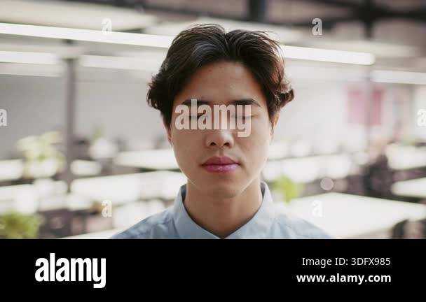 A young Asian man sits quietly in a contemporary office space. The ...