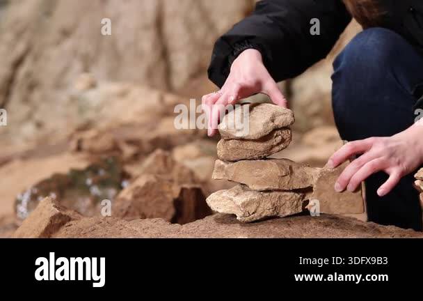 A woman stacks stones one on top of the other, making a wish. Stacking ...