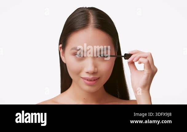 A beautiful young woman is pampering herself as she applies mascara ...