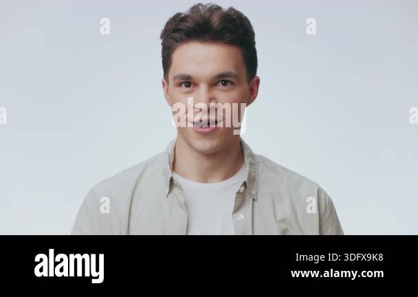 A young guy with a charming smile poses in front of a light background ...