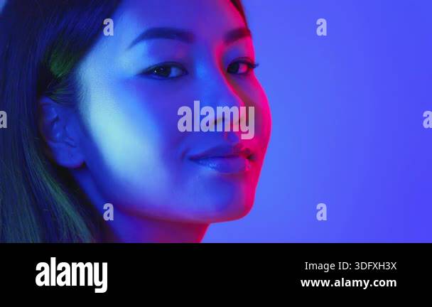 A young Asian woman poses confidently against a vibrant neon background ...