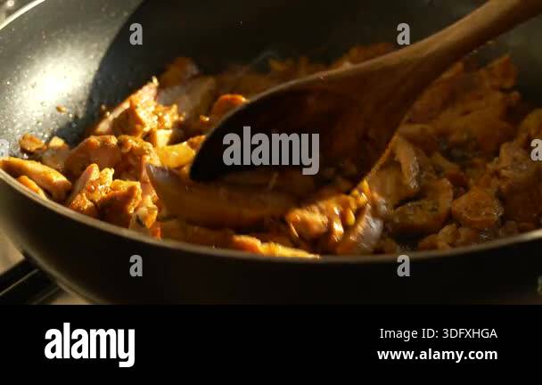 Detailed shot of juicy meat cooking in a pan. Wooden spoon stirring ...