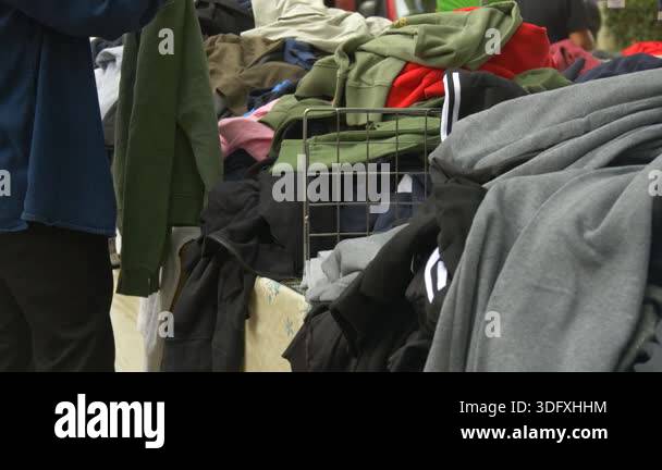 A mans hand searching through a mix of second hand clothes in different ...