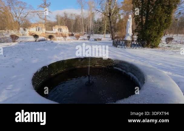 A fountain stands in a snowy winter park, framed by architectural ...