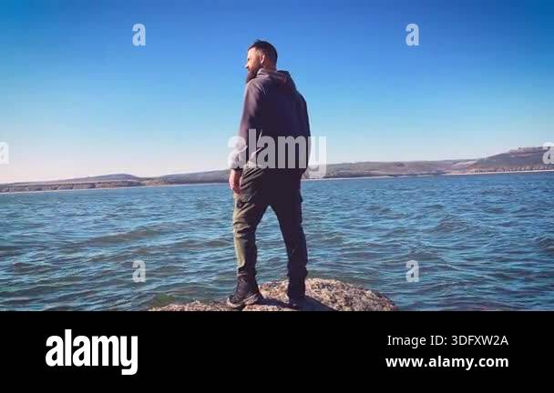 Young attractive tourist standing on the rocky shore of a mountain lake ...