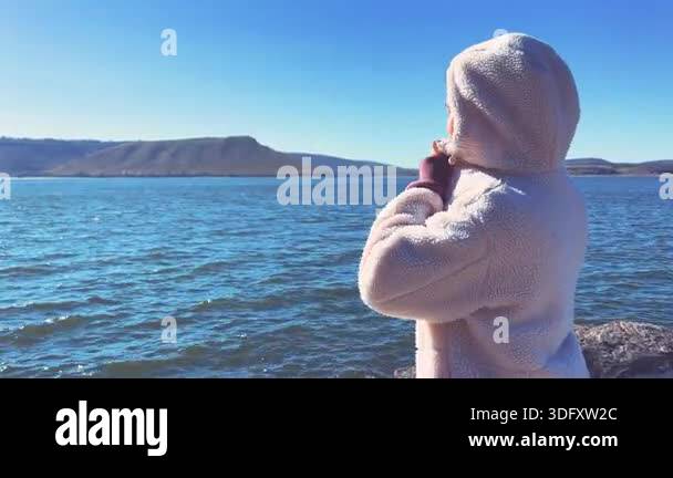 Young attractive girl traveler standing on the rocky shore of a ...