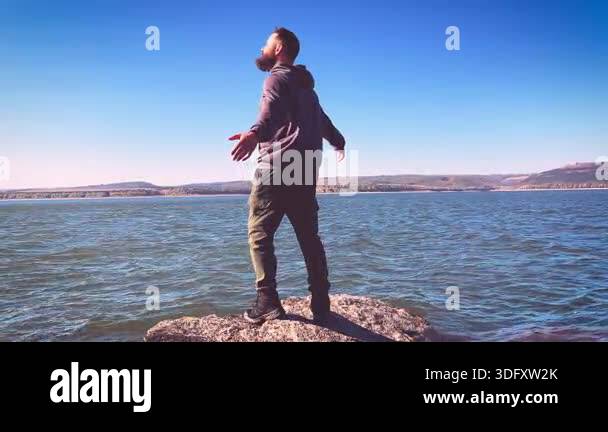Young attractive tourist standing on the rocky shore of a mountain lake ...
